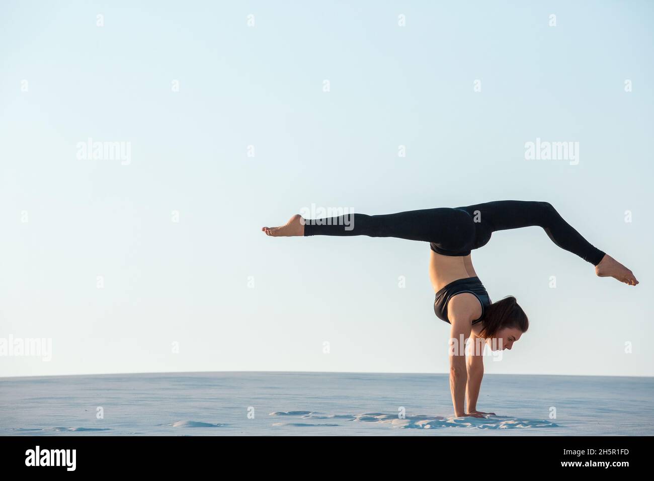 Young woman practicing inversion balancing yoga pose handstand on sand ...