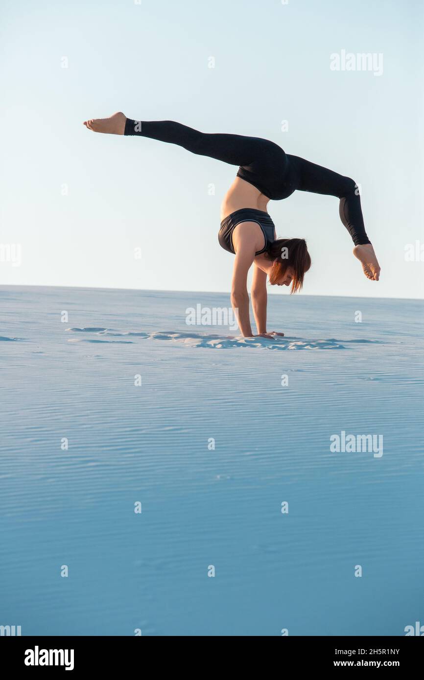 Young woman practicing inversion balancing yoga pose handstand on sand ...