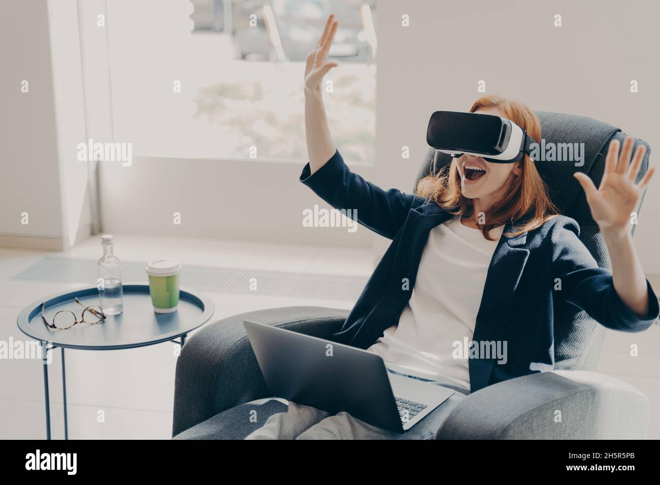 Young excited redhead woman testing VR glasses or goggles while sitting ...