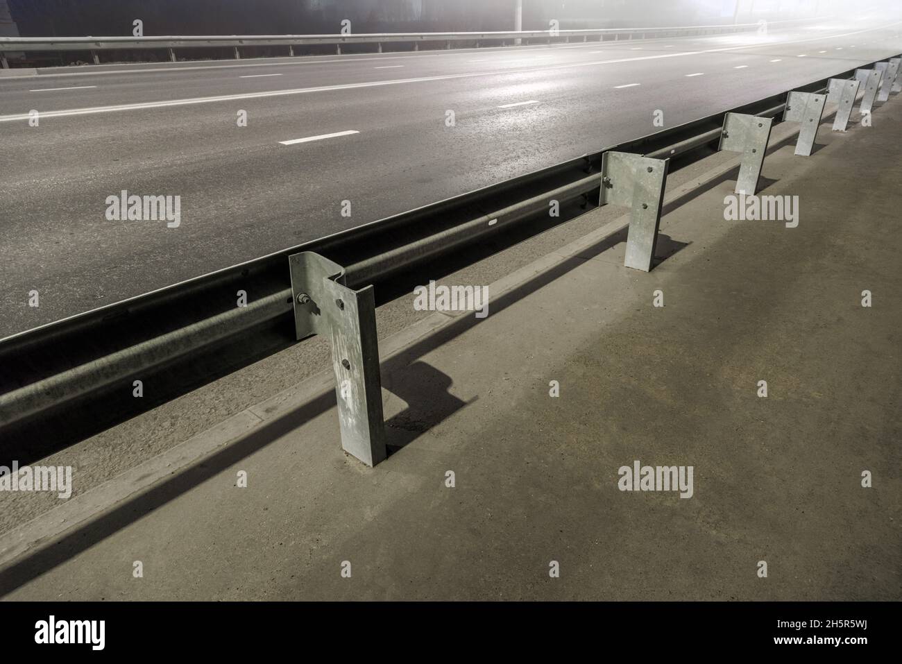 illuminated empty foggy night road with rigid guardrails, traffic ...
