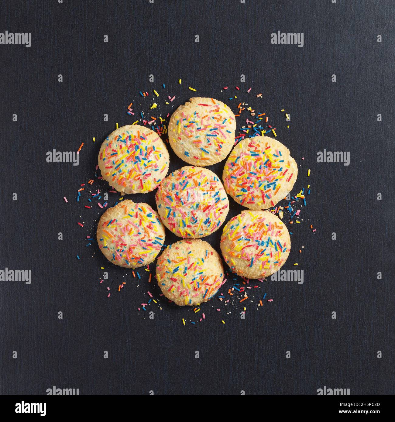 Cookies with colorful sprinkles on black stone background, top view ...