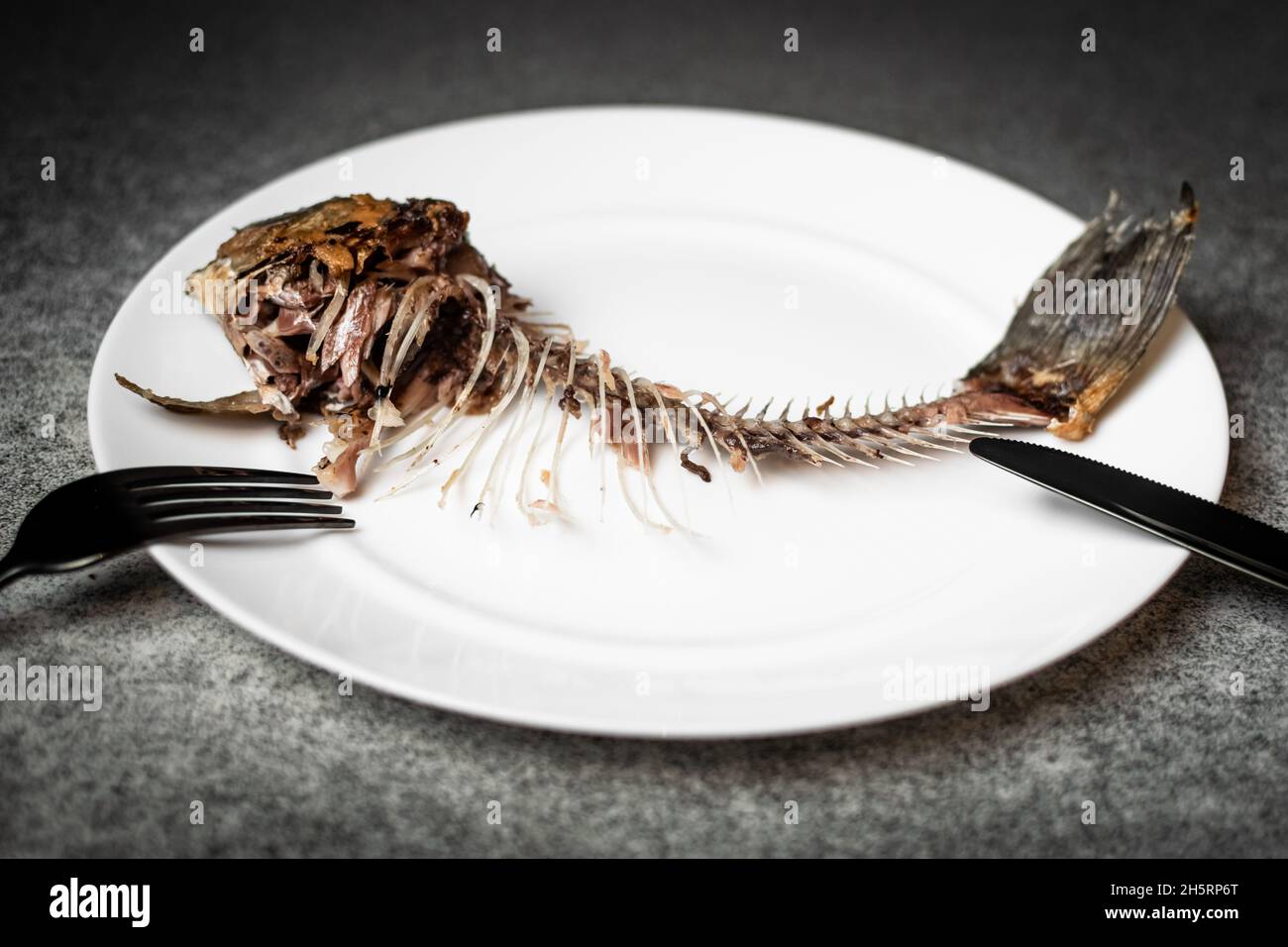 Fried fish skeleton, spine and bones on a white plate with a black ...