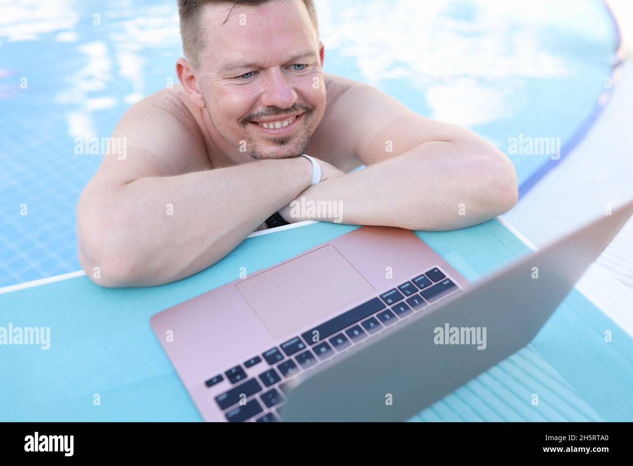 Man lying on side of swimming pool and looking at laptop screen Stock ...