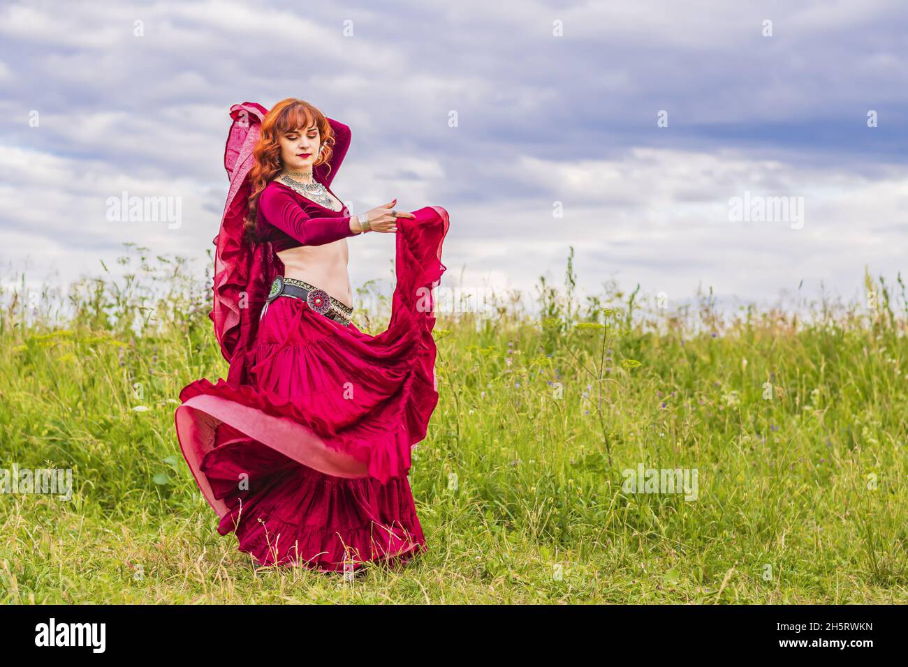 Red-haired young woman in red dress dancing beautiful dance under open ...