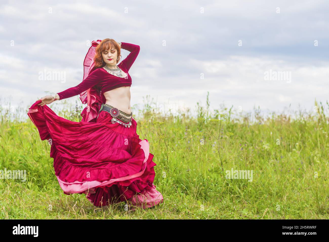 Red-haired young woman in red dress dancing beautiful dance under open ...