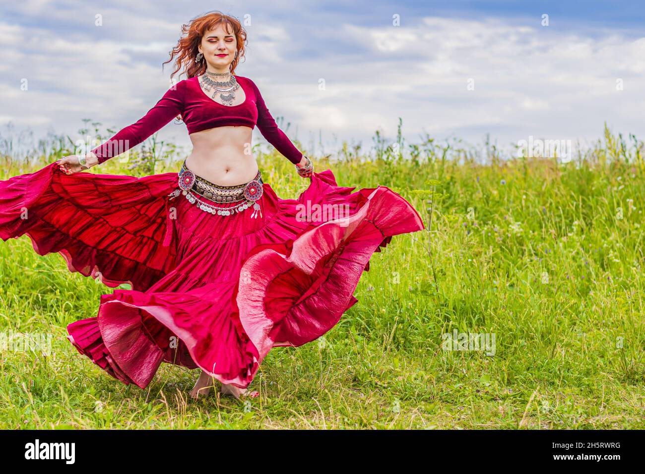 Red-haired young woman in red dress dancing beautiful dance under open ...