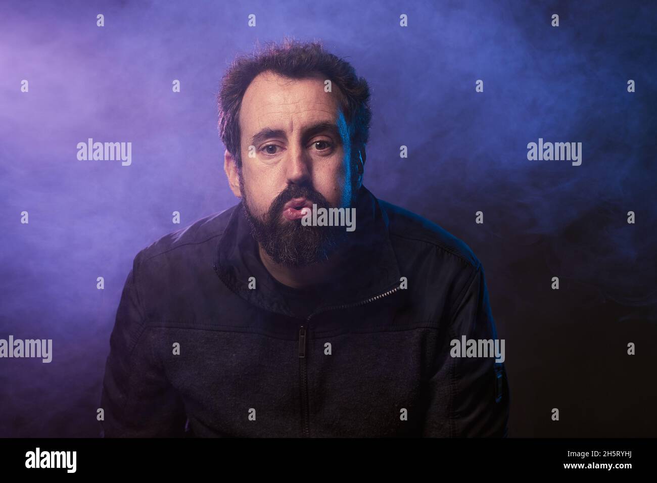 portrait of attractive man blowing into the camera with colored smoke ...