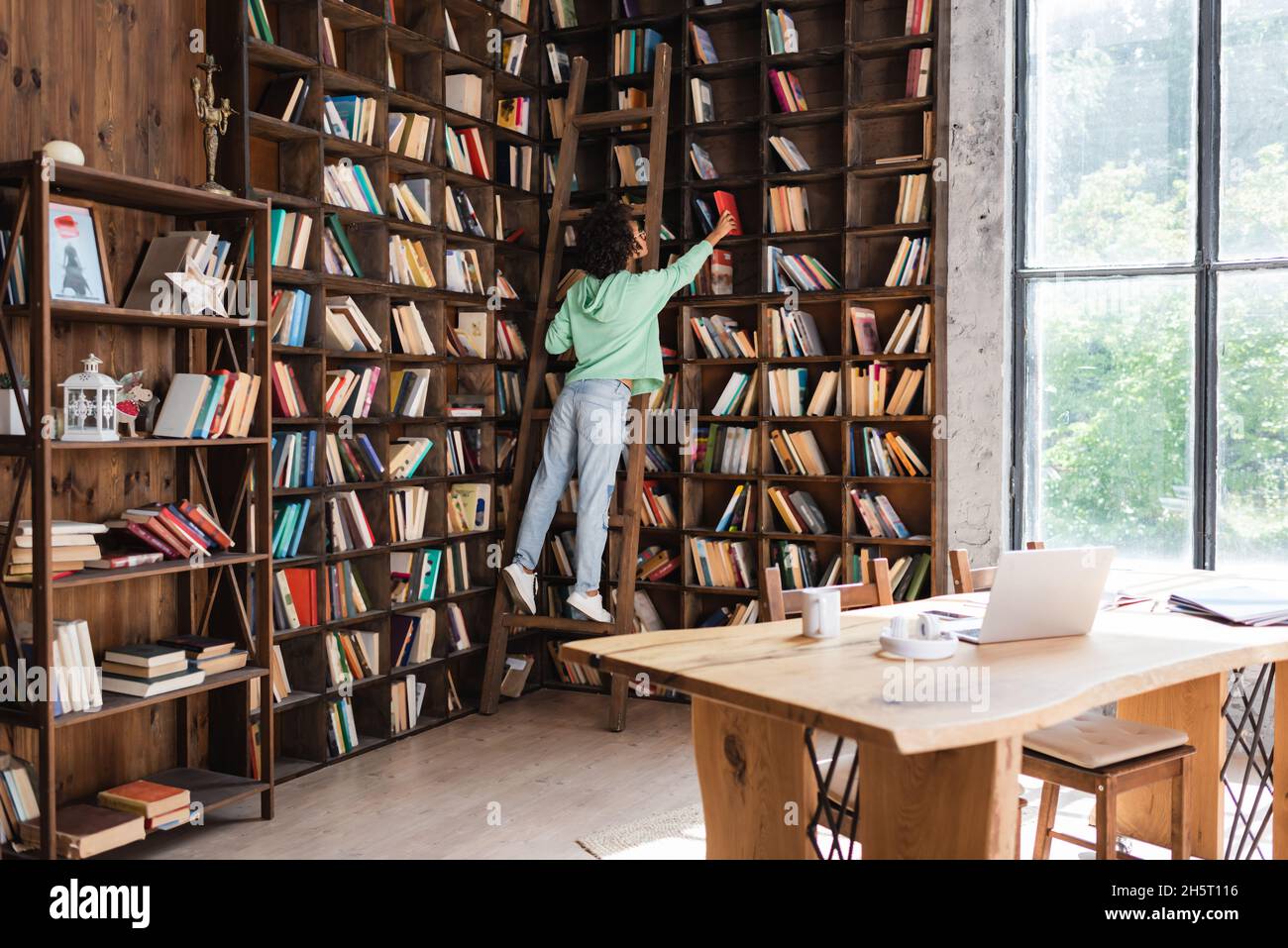 african american student standing on wooden ladder while reaching book ...