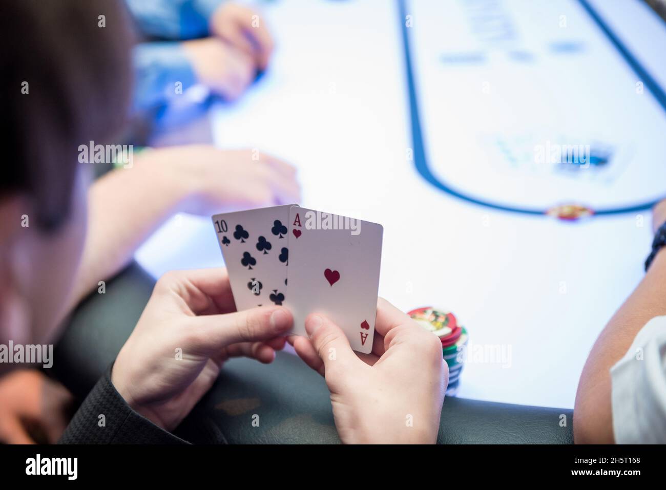 Over-shoulder shot of poker cards in player hands on a gaming board ...