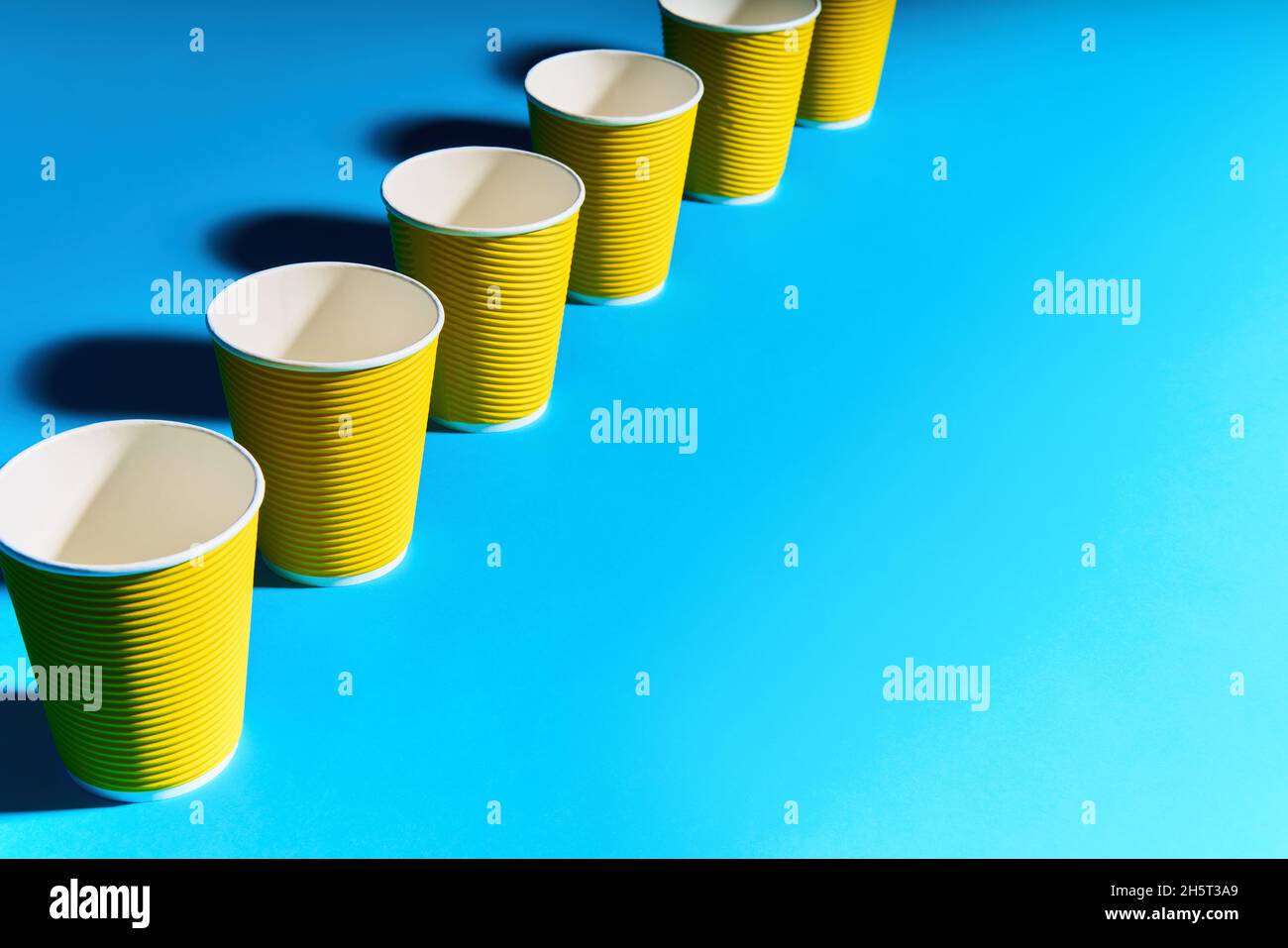 Diminishing perspective of yellow paper cup in row on blue background ...