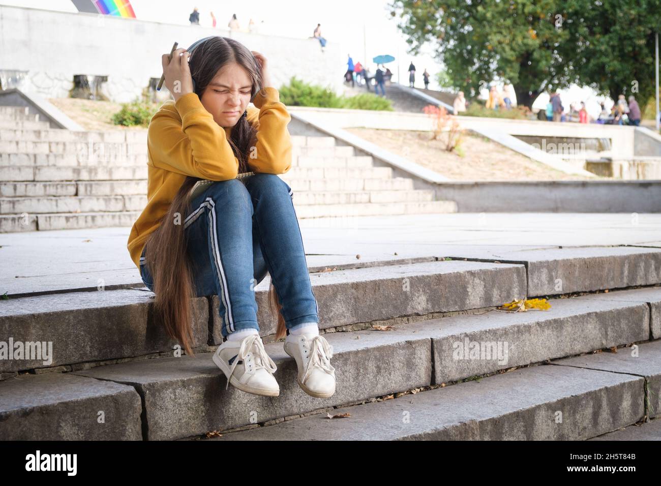 A sad teenage girl sits on the stairs and covers her head with her ...