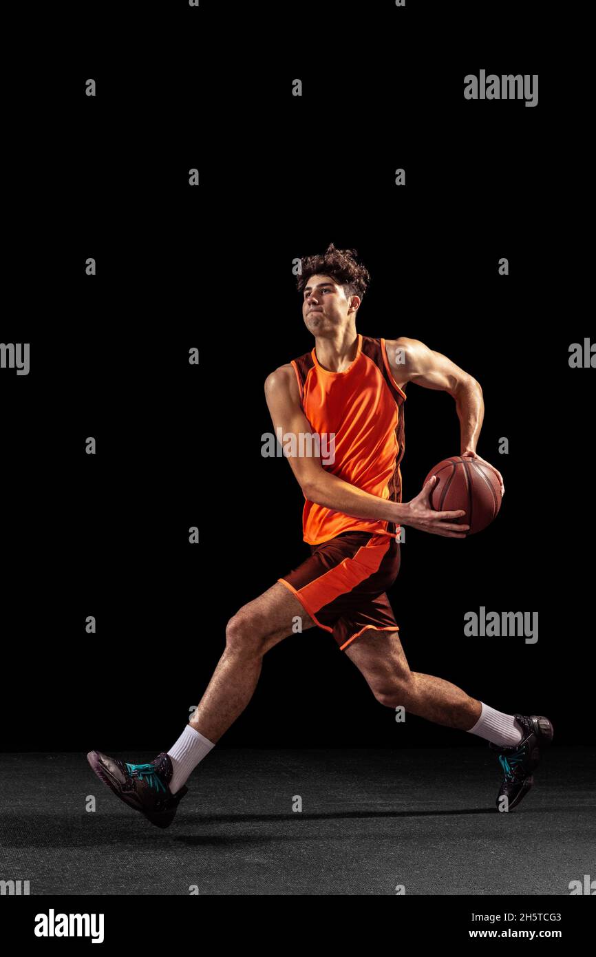 Full length portrait of basketball player training isolated on dark ...