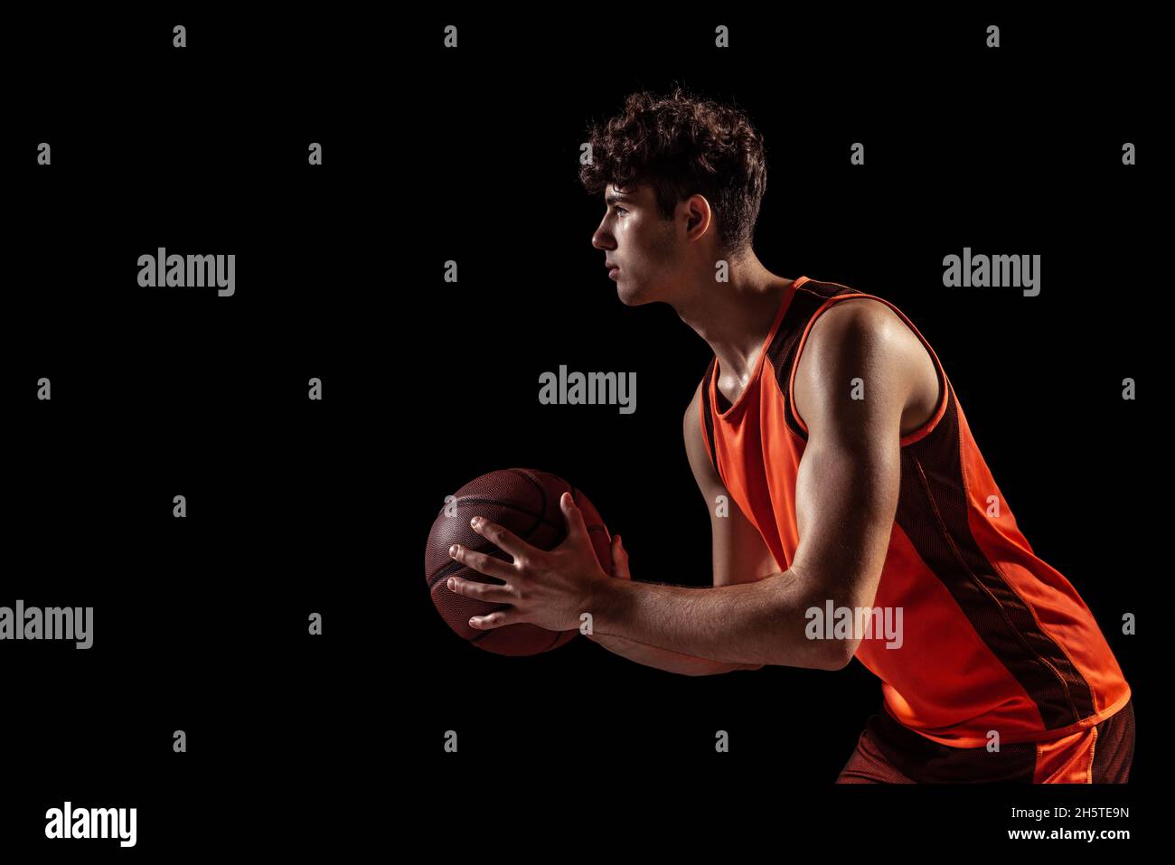 Profile view of basketball player posing with ball isolated on dark ...