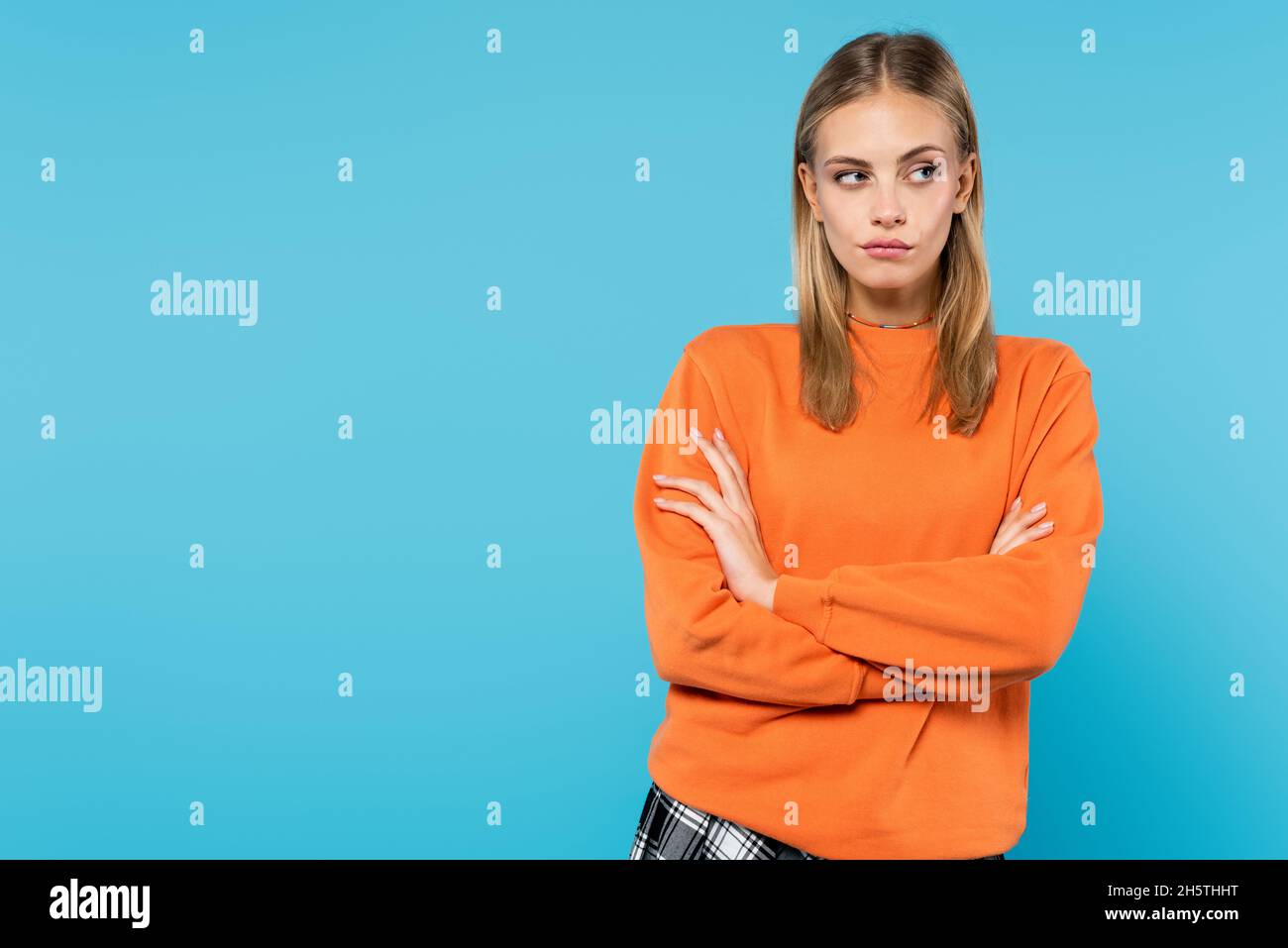Skeptical woman standing with crossed arms isolated on blue Stock Photo ...