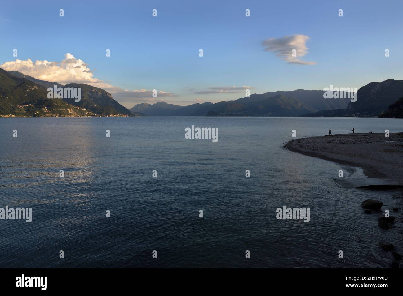 View of two anglers at the shady lake shore and opposite the village ...