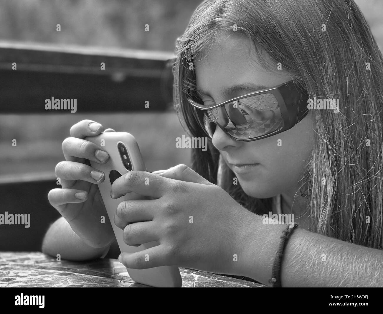 Grayscale shot of an Italian girl sitting outdoors wearing sunglasses ...