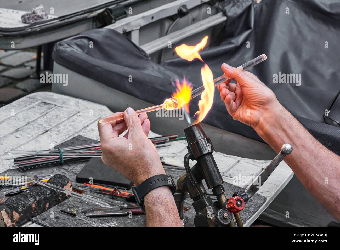 Hands of mature glassblower holding glass rod over burner flame ...
