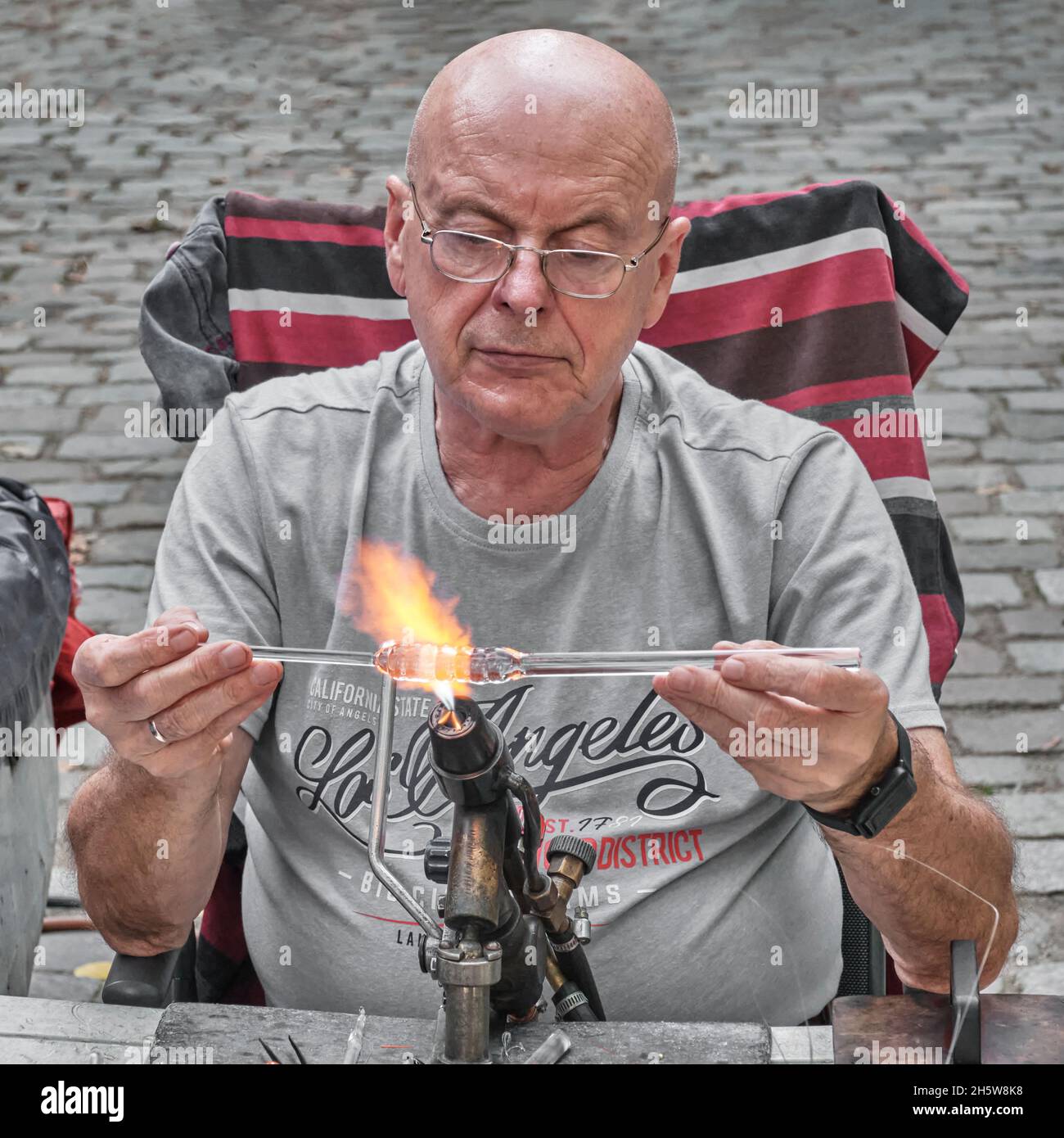 Hands of mature glassblower holding glass rod over burner flame ...