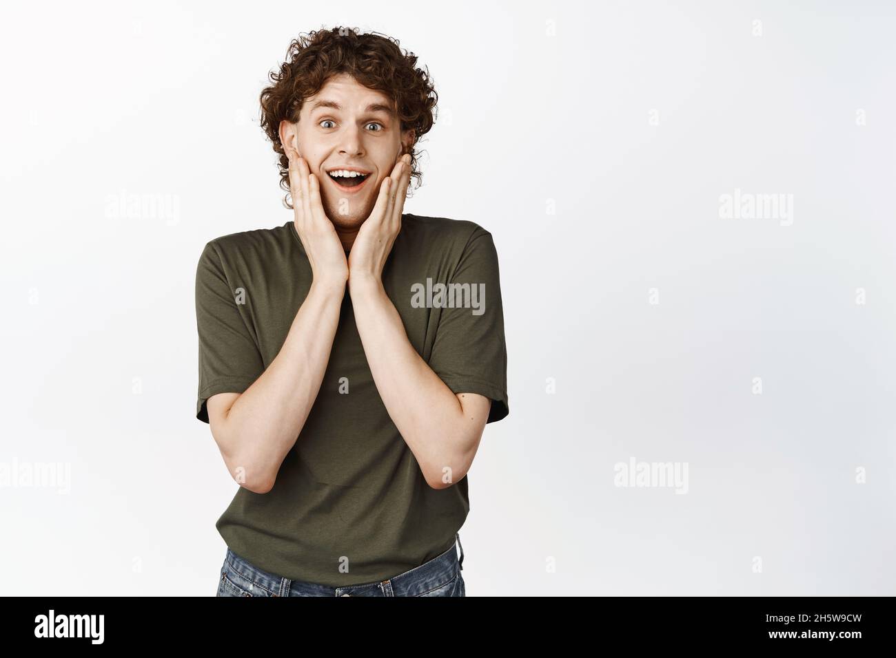 Happy handsome curly-haired man, cupping his face in hands, smiling and ...