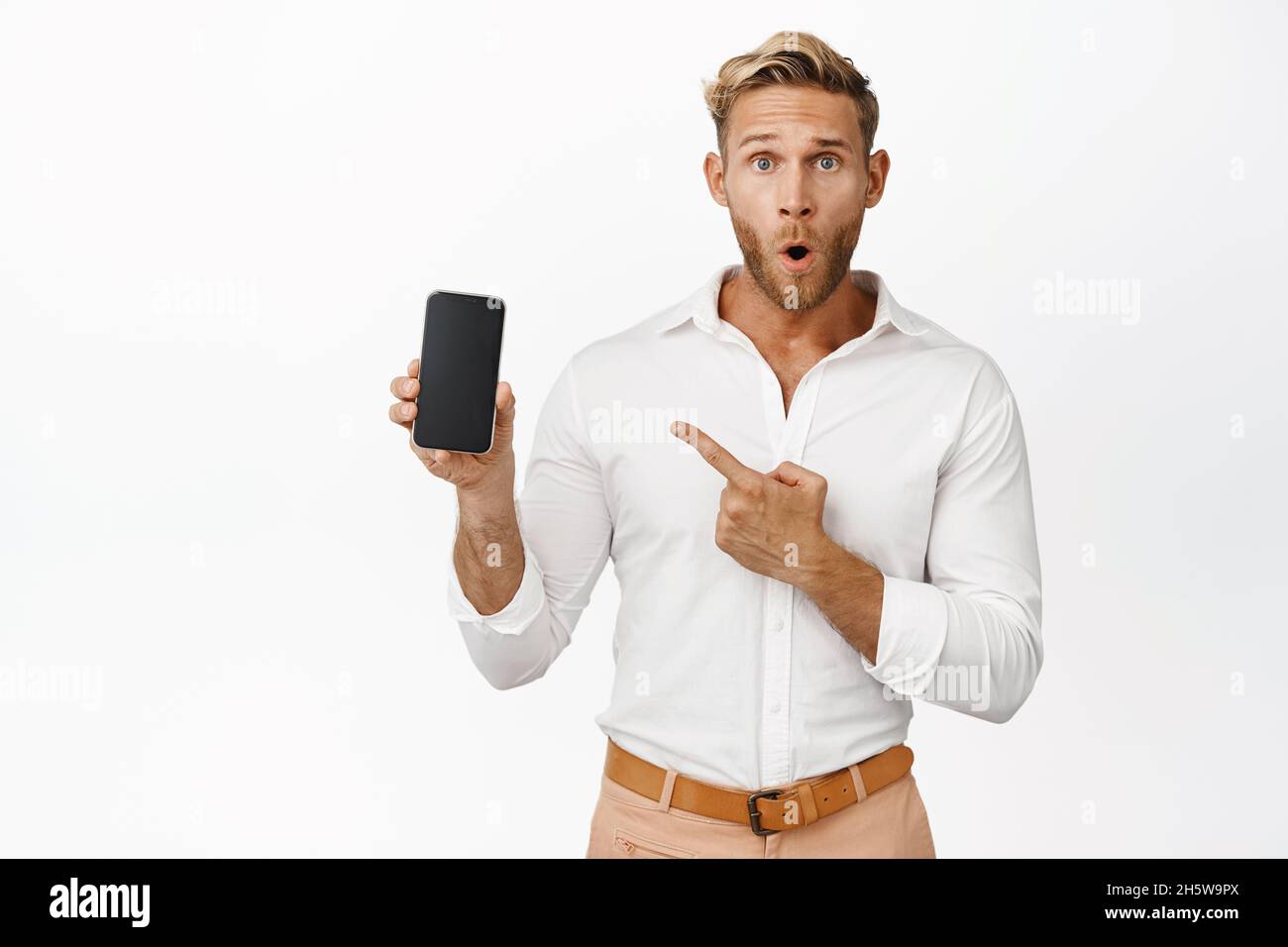 Portrait of impressed man pointing at phone and saying wow, showing ...
