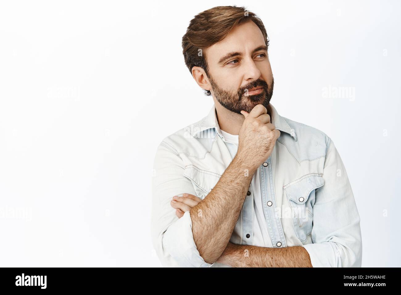 Thoughtful caucasian guy looking aside and touching his beard, thinking ...