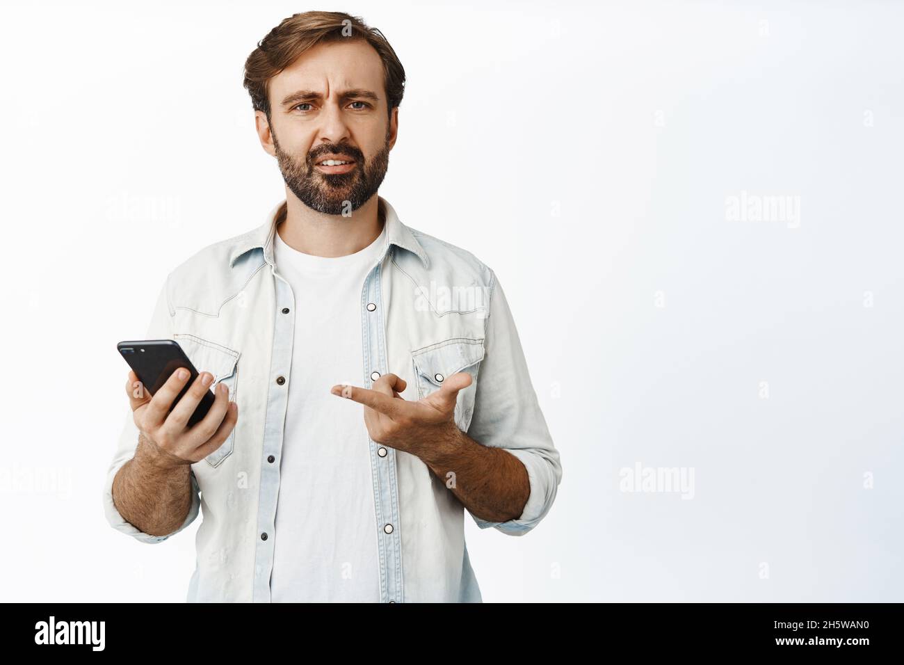 Confused bearded man pointing at his phone and asking question, need ...