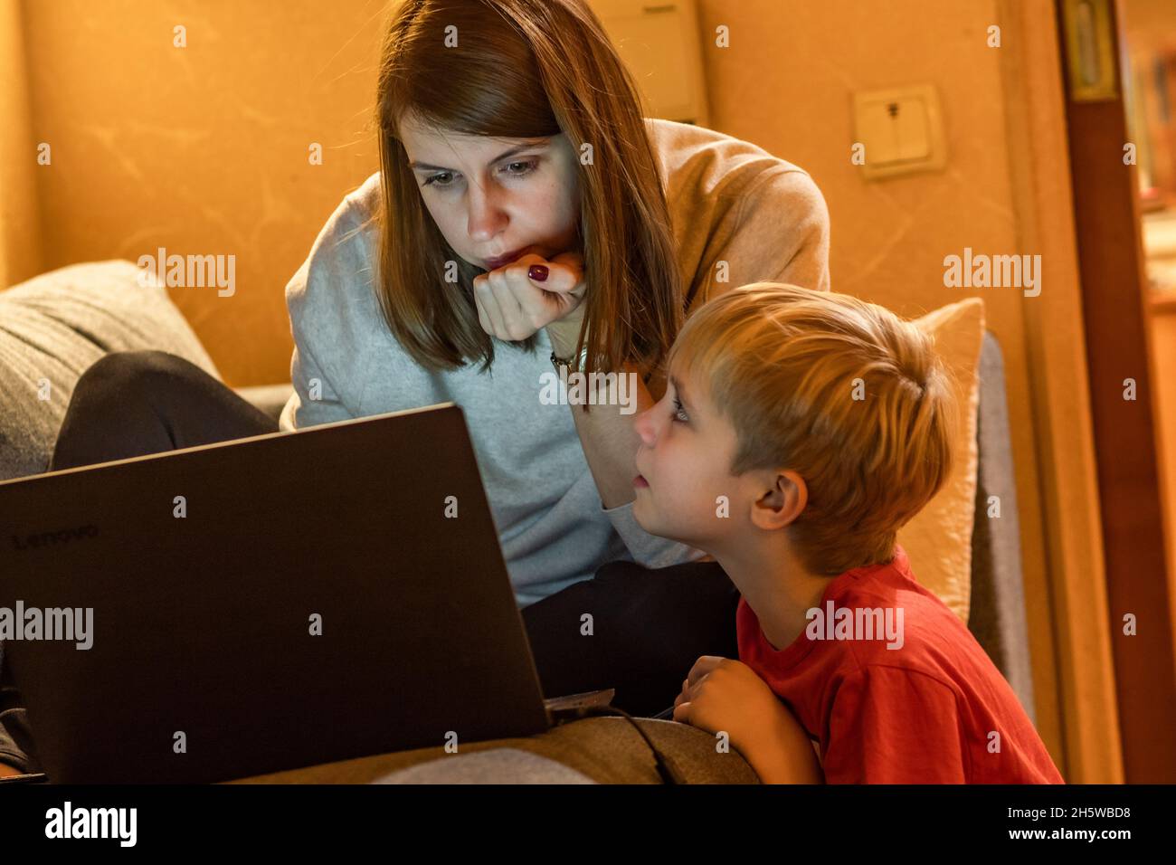 Russia, Moscow. A little boy in the living room while his mother works on a laptop in the home ...