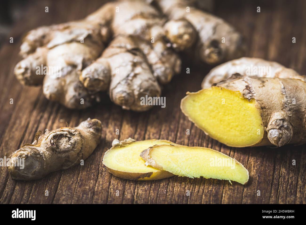 Fresh ginger on a wooden board, whole roots and cut slices, close-up ...