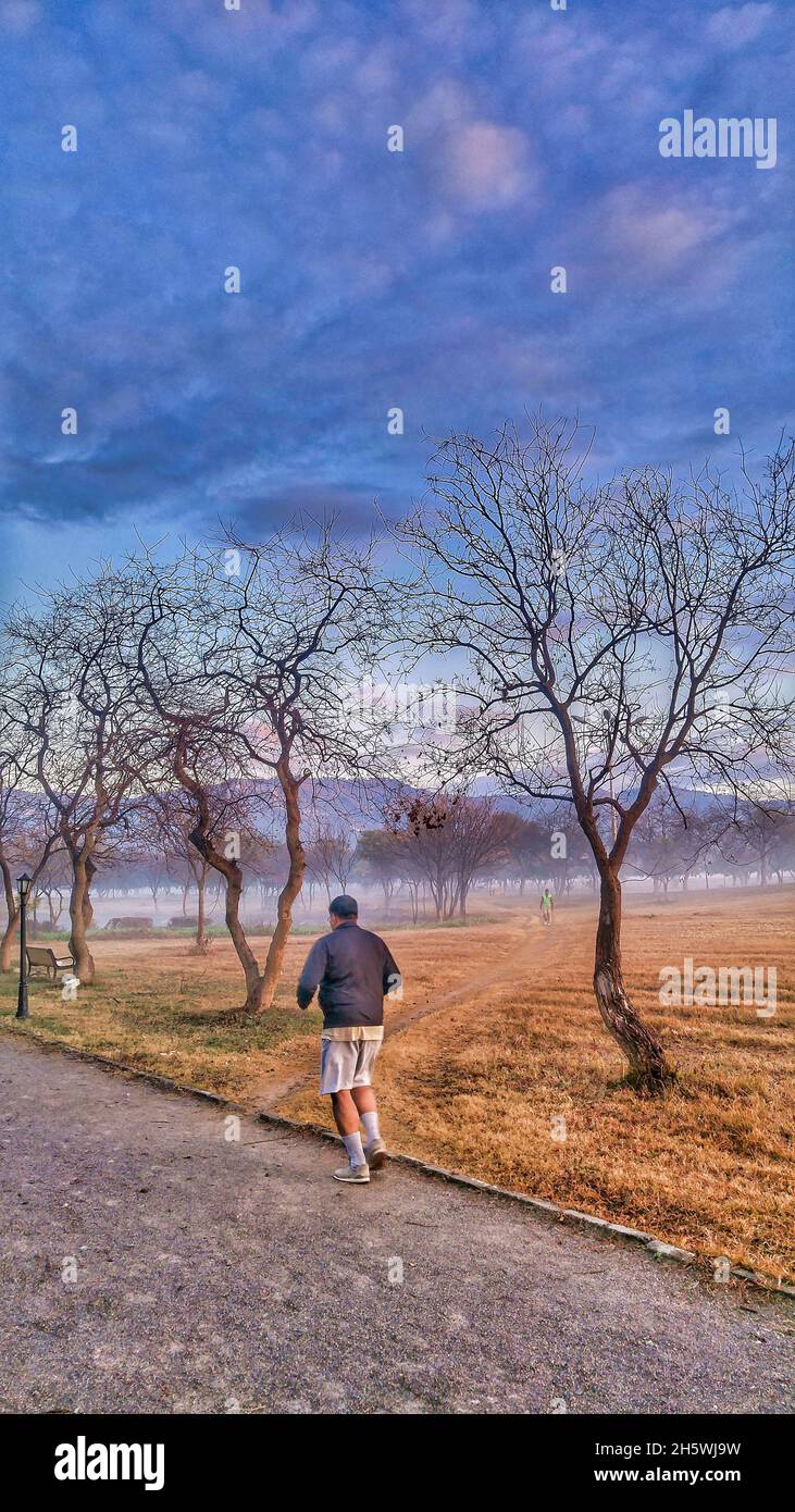 Person jogging on a track in a park with the beautiful sky on a cold ...