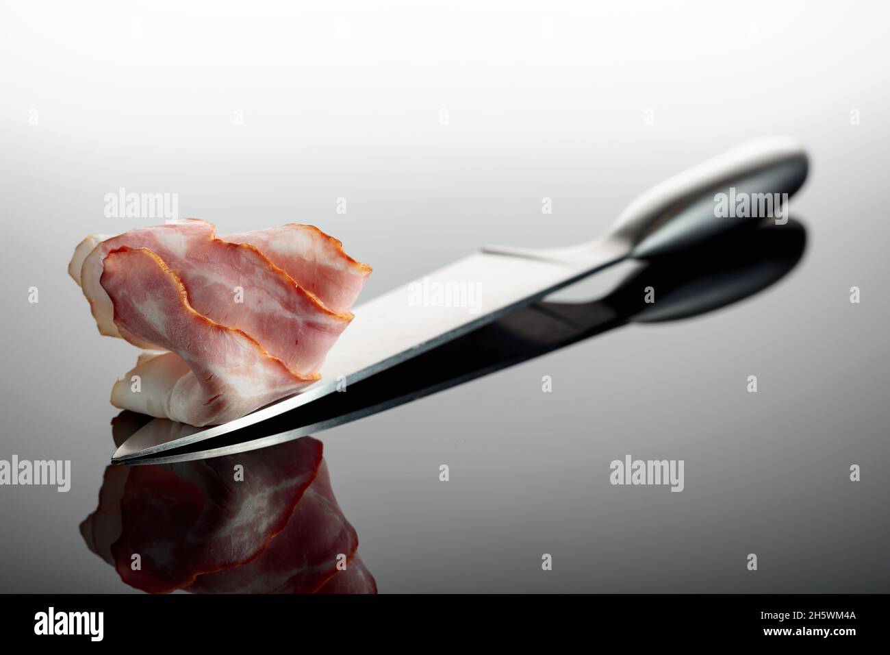 Bacon slices on a kitchen knife. Reflective background Stock Photo - Alamy