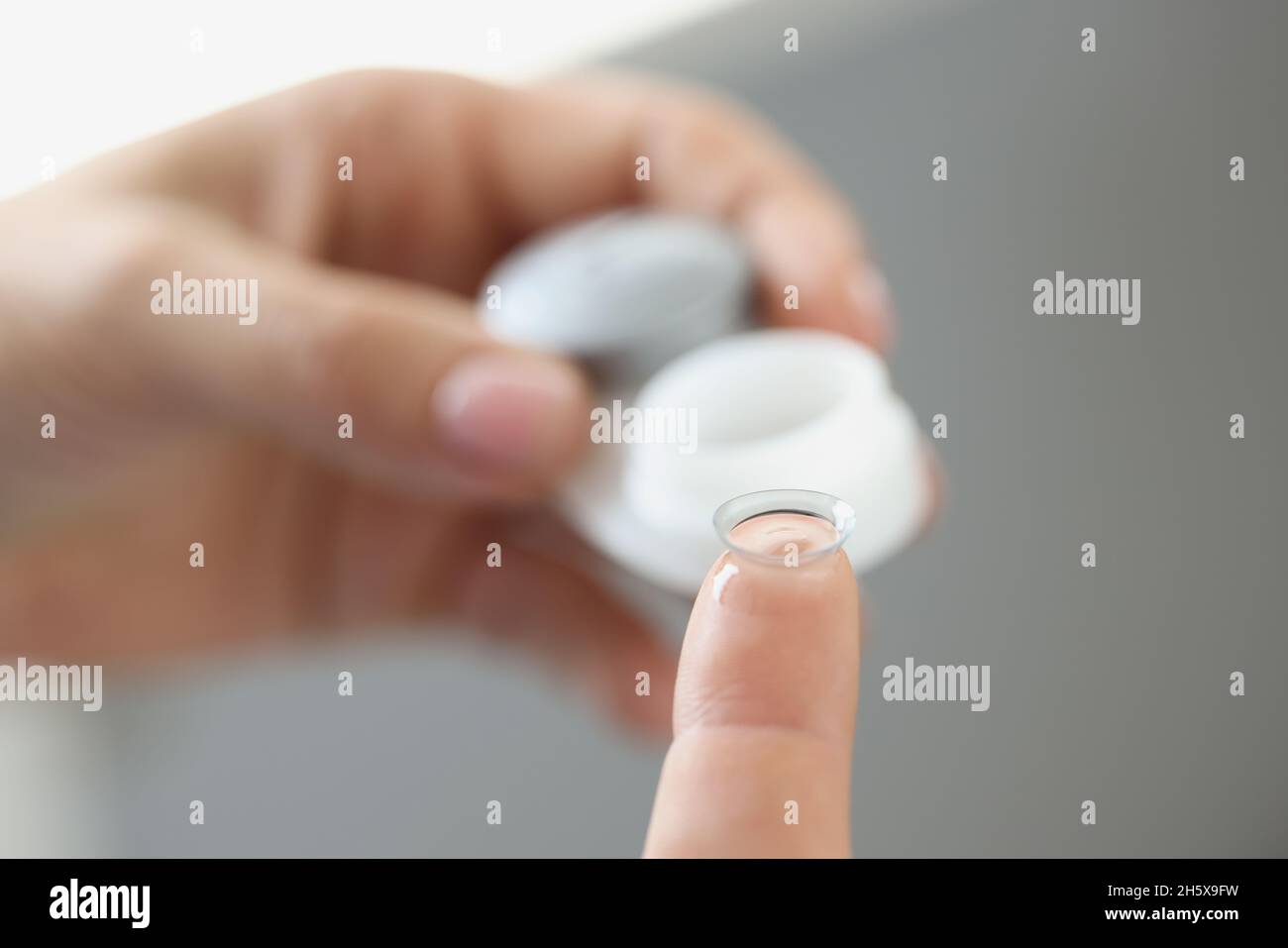 Woman pulling contact lens out of plastic container with her finger ...