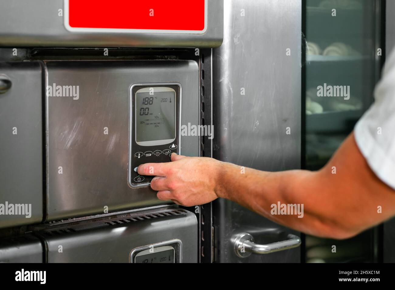 Crop unrecognizable male baker pushing buttons of modern metal oven ...