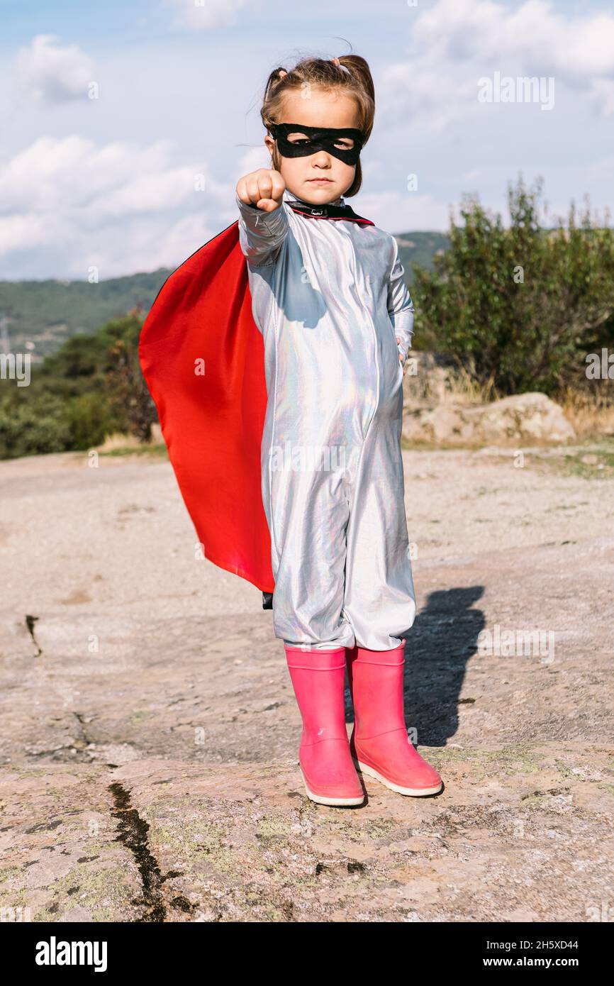 Full body of small girl in superhero costume raising outstretched fists ...