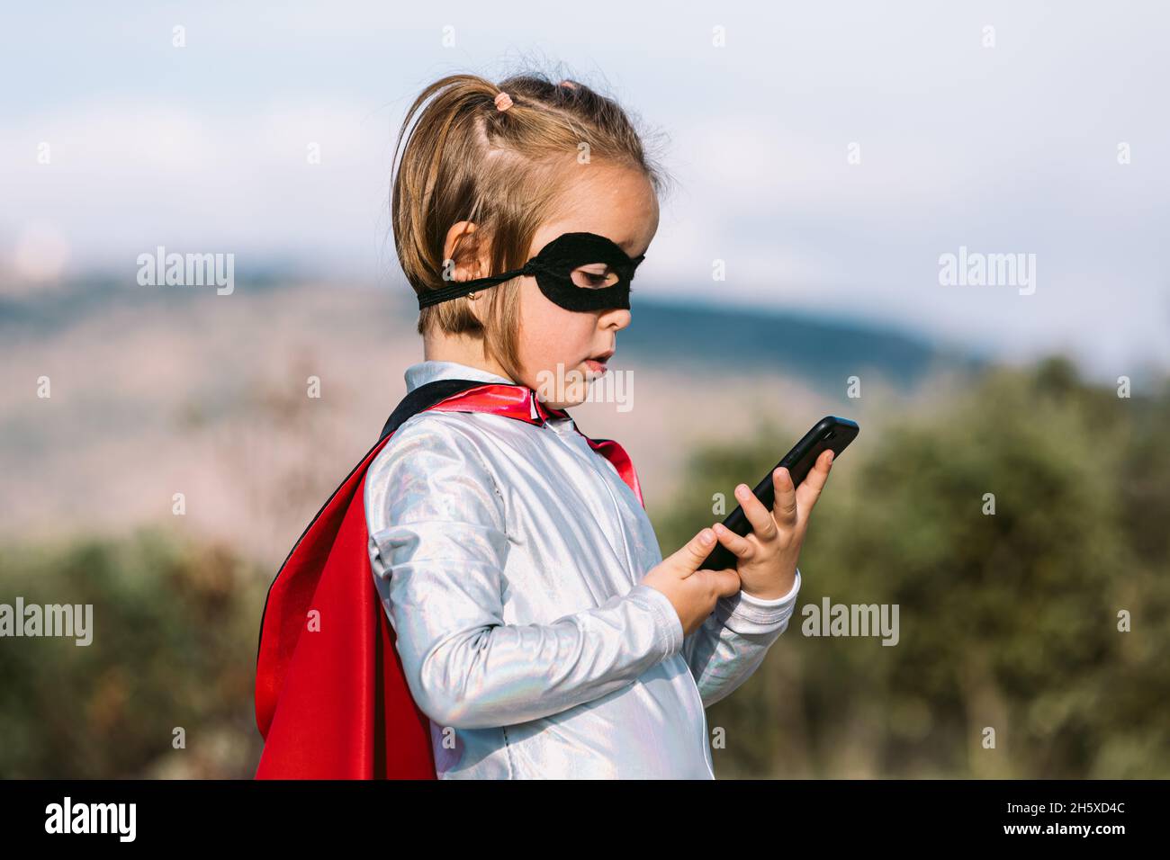 Side view of self assured girl in eye mask superhero costume with cape ...