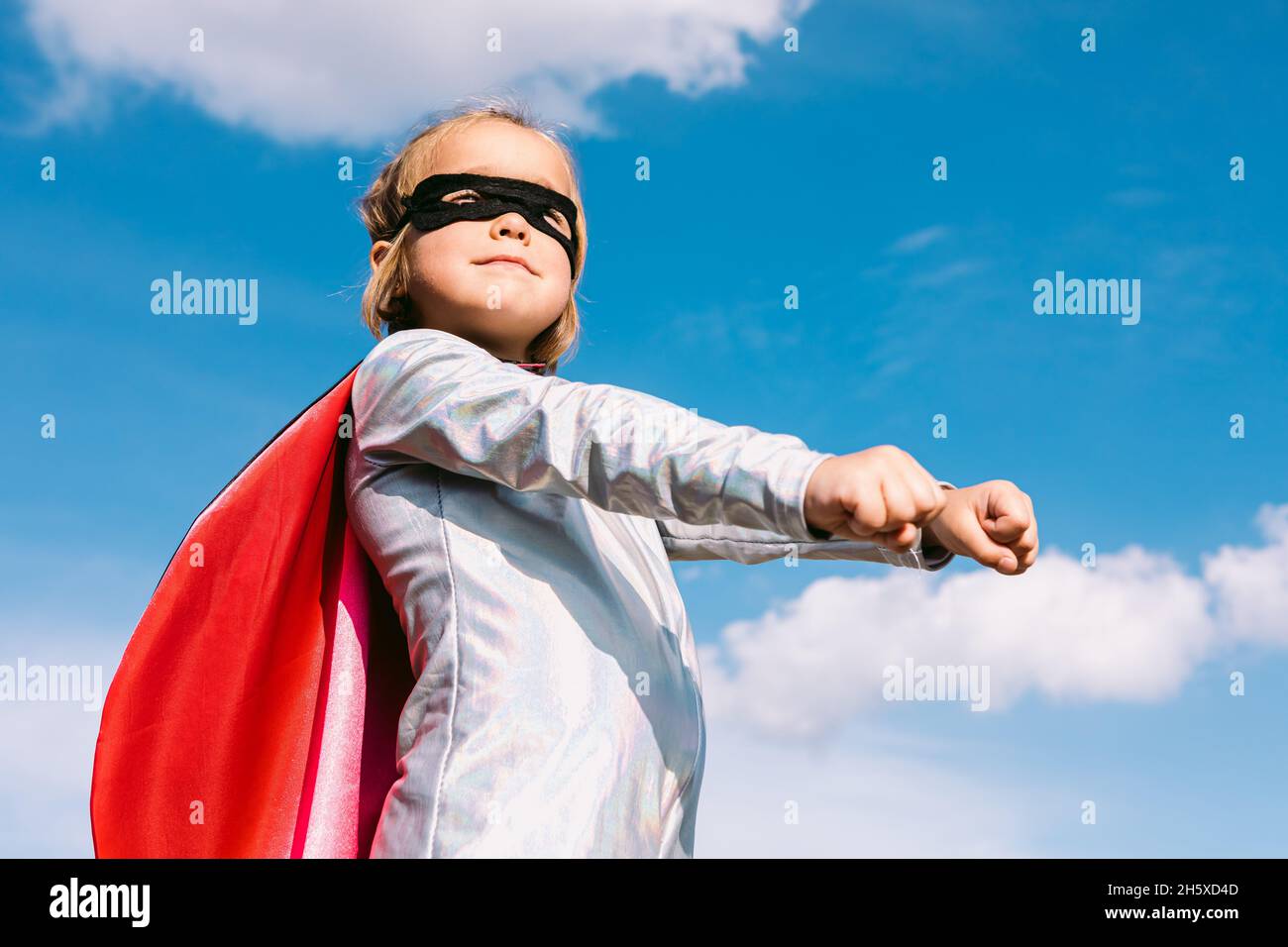 From below small girl in superhero costume raising outstretched fists ...