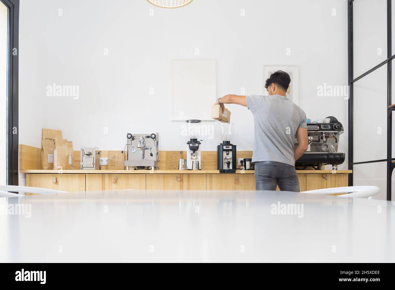 Back view of anonymous male barista pouring coffee beans from bag into ...