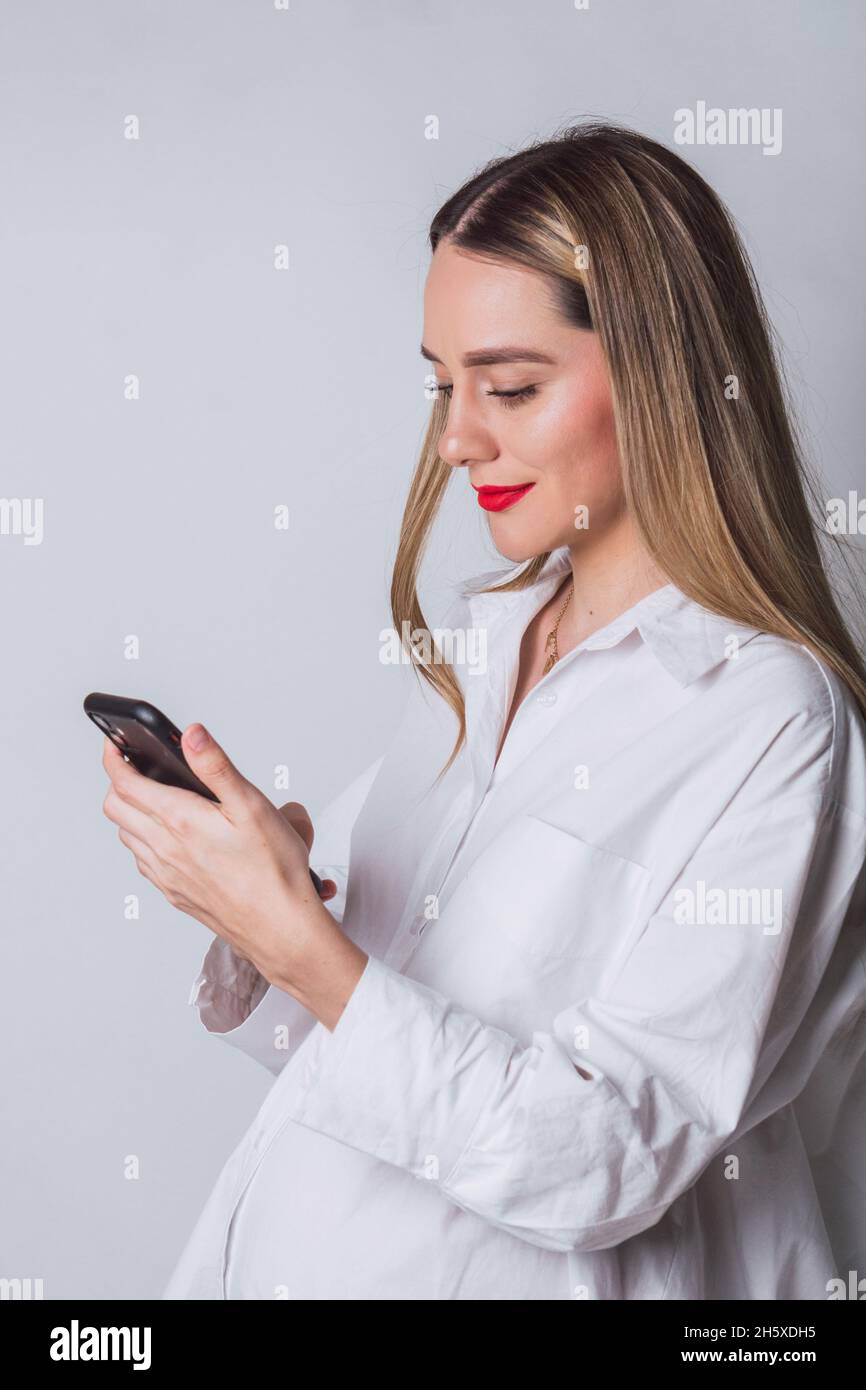 Positive young pregnant female with red lips in white shirt texting on ...