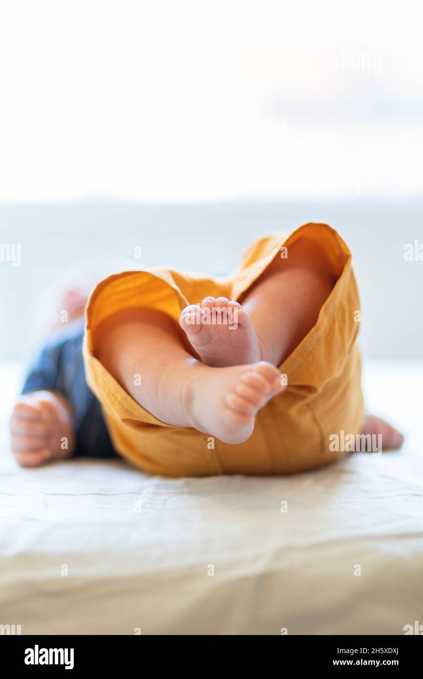 Anonymous cute barefooted baby lying alone on comfortable bed in sunny ...