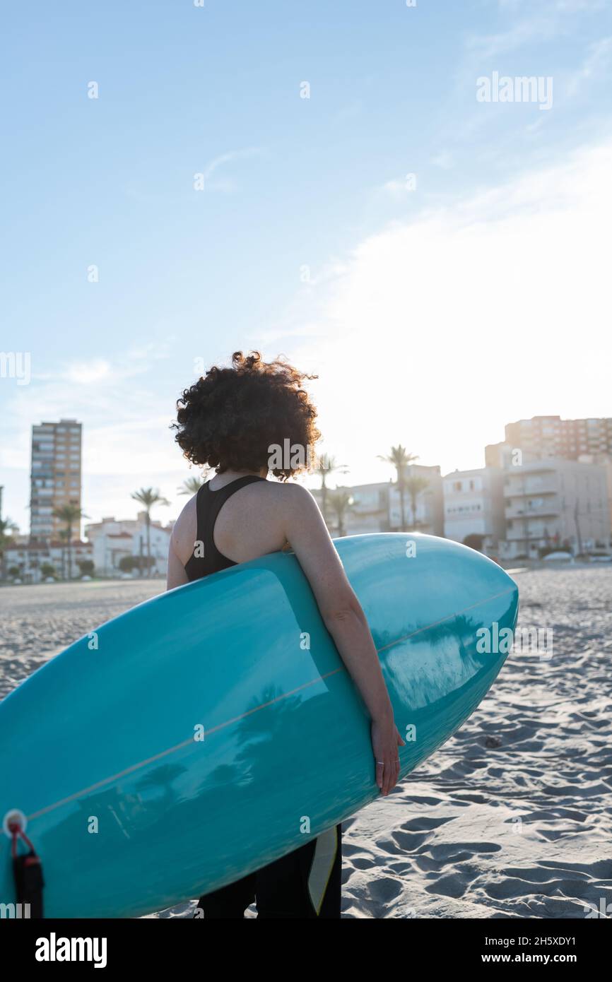 Back view of unrecognizable female surfer in wetsuit with surfboard ...