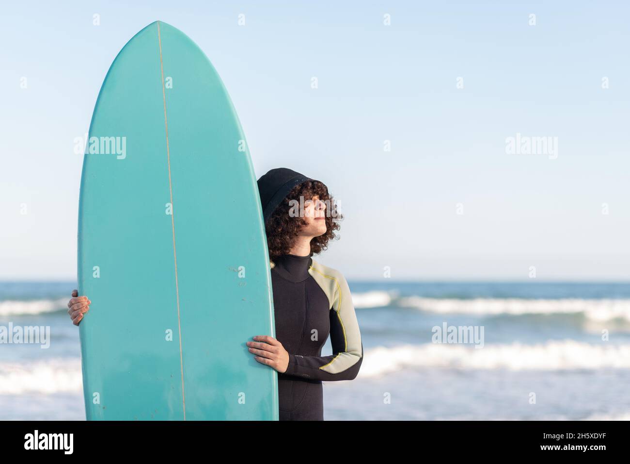Side view of young thoughtful female surfer in wetsuit with surfboard ...