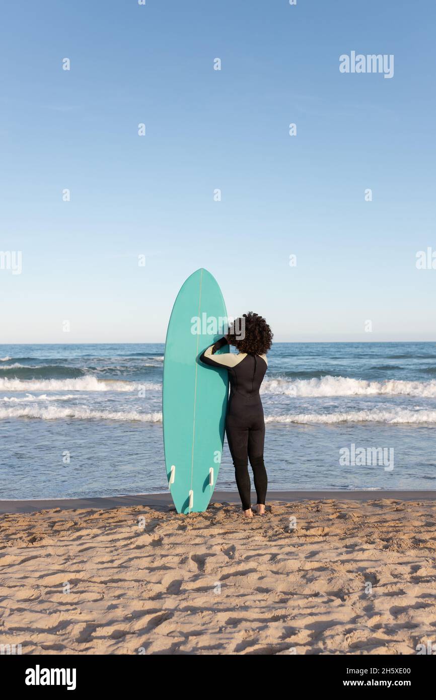 Back view of unrecognizable female surfer in wetsuit with surfboard ...