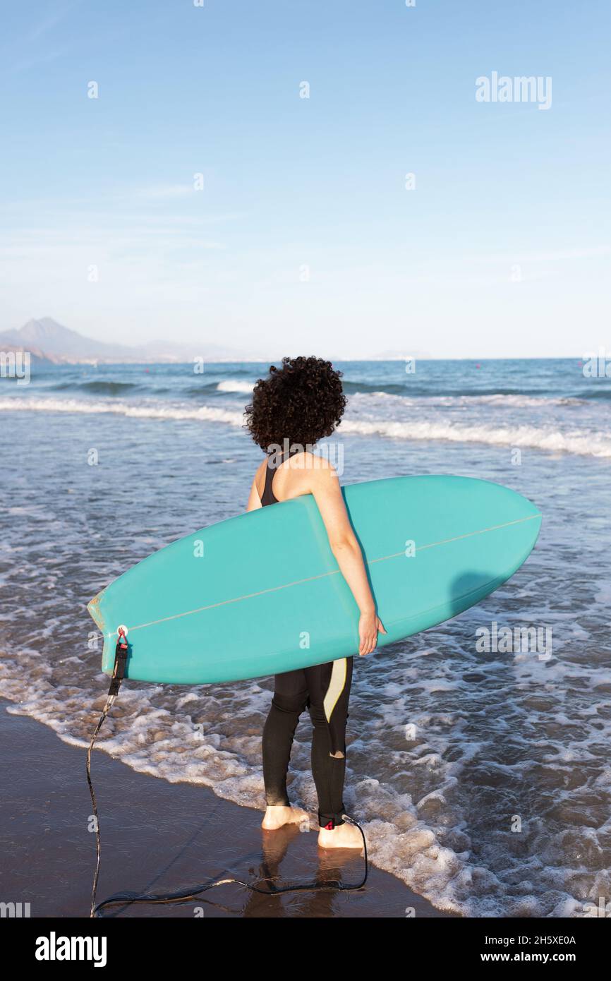 Back view of unrecognizable female surfer in wetsuit with surfboard ...