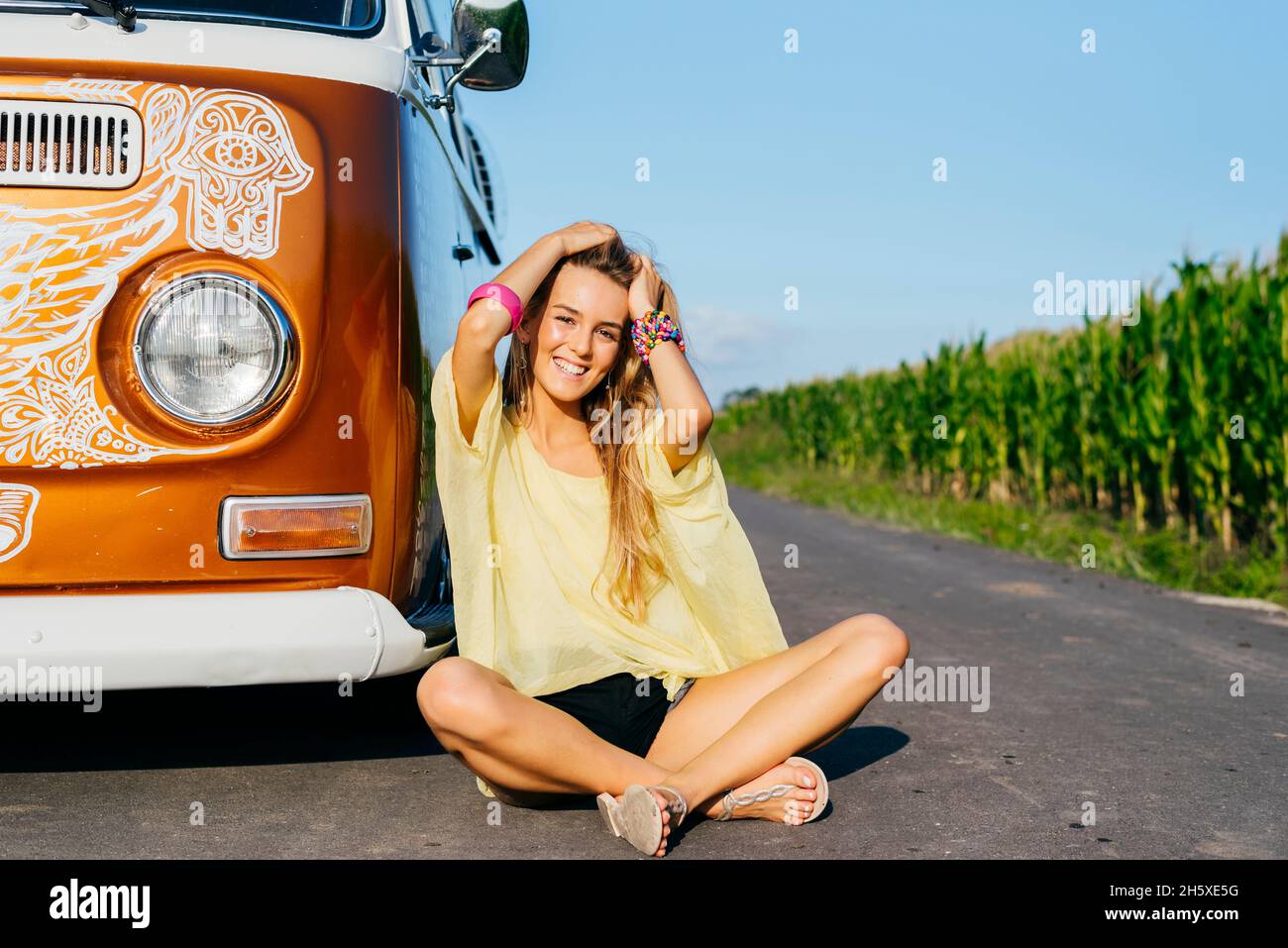 Beautiful happy blonde girl outside a van sitting on the road looking ...