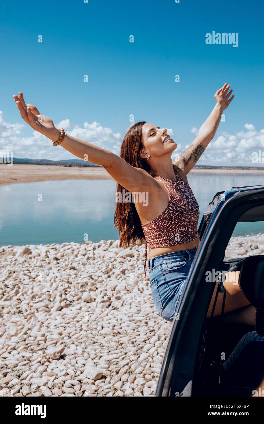 Side view of young female in denim jeans and top leaning out of car ...