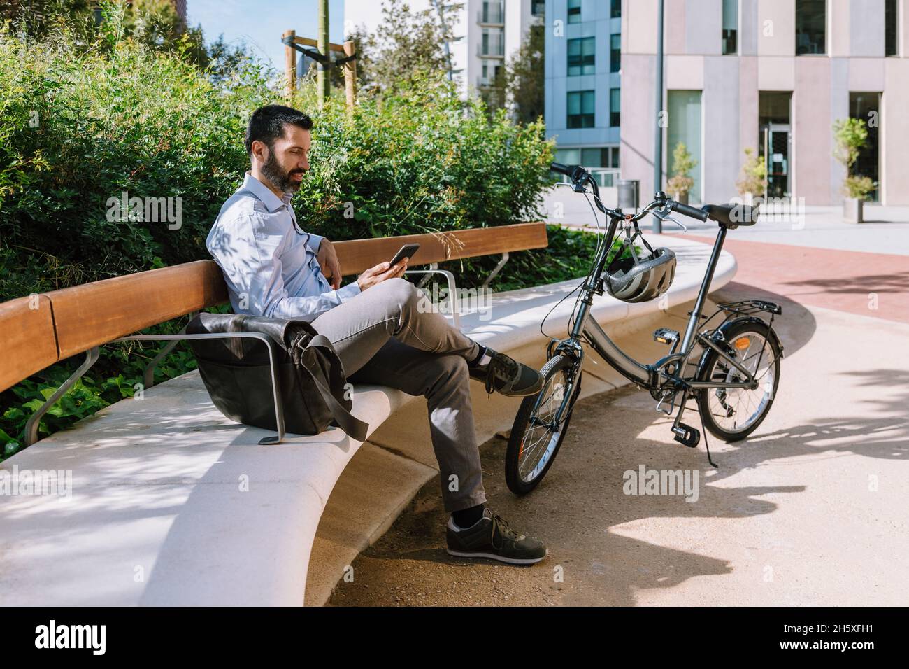 Full body side view of male manager sitting on bench near bicycle and ...