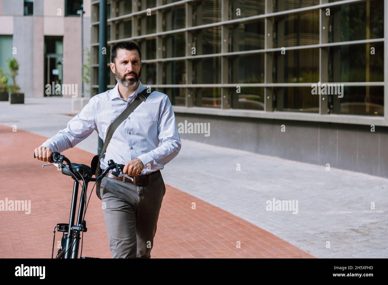 Executive worker in formal wear standing with bicycle near modern ...