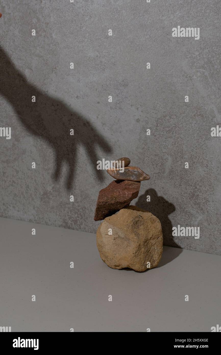 Vertical shot of balanced stones with a shadow of a hand reaching out ...