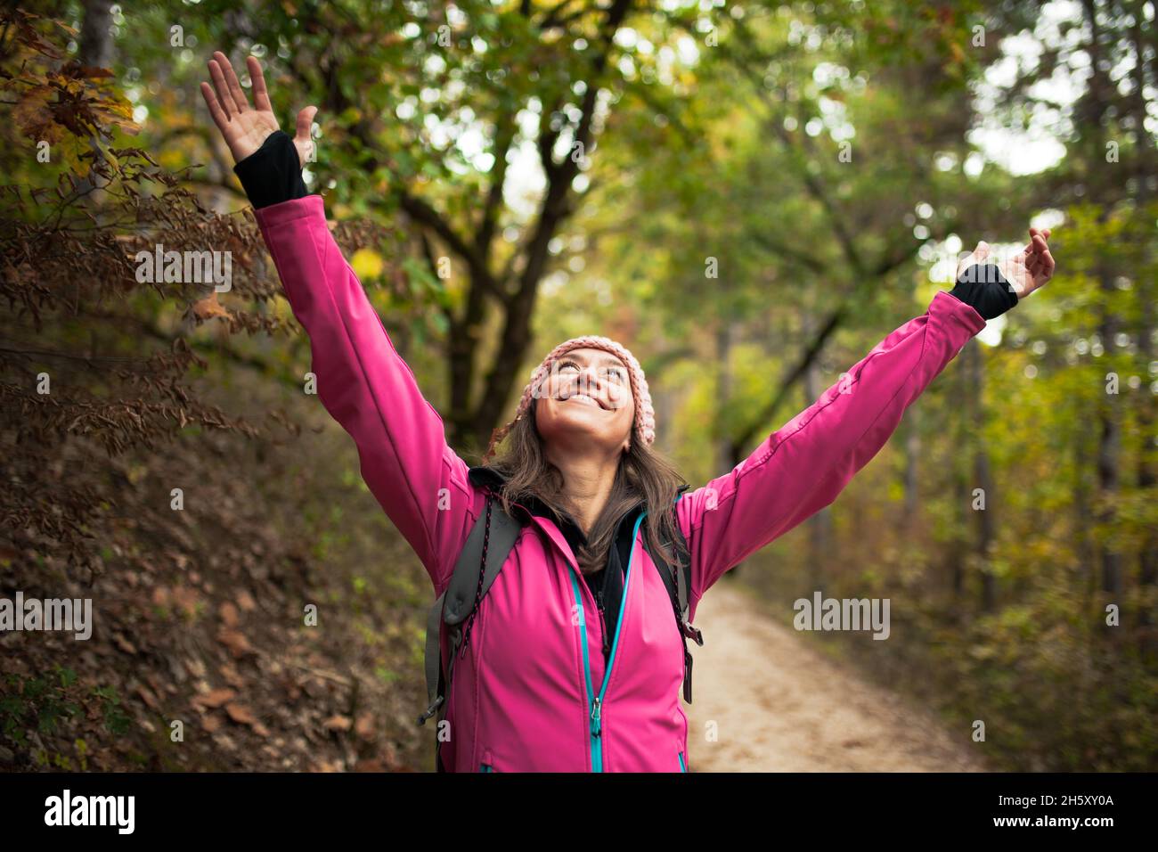 Hiking girl in pink on a trail in the forest. Hands up enjoying the ...