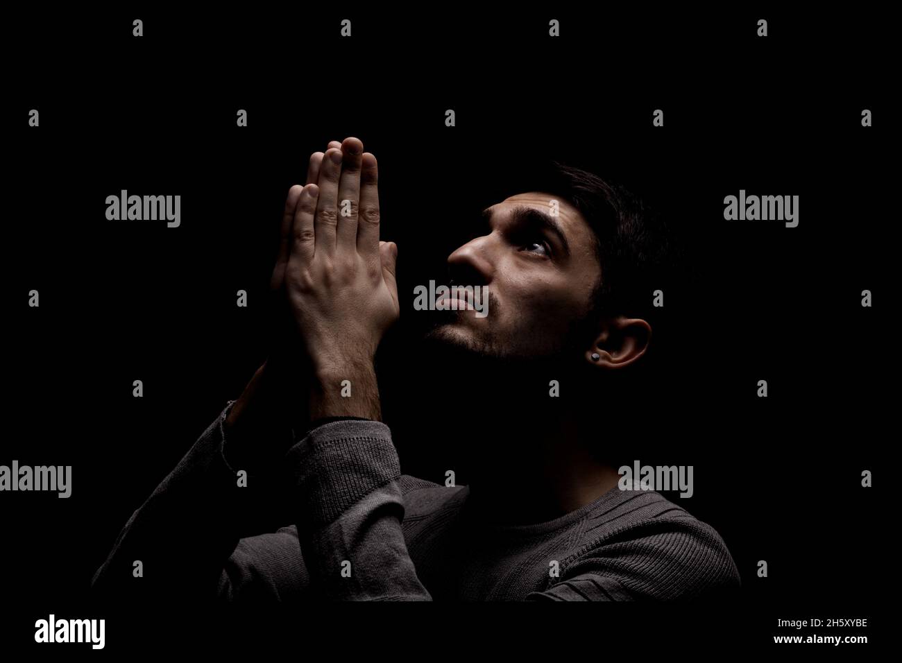 Headshot of serious confident young man praying in dark room. Lit from ...