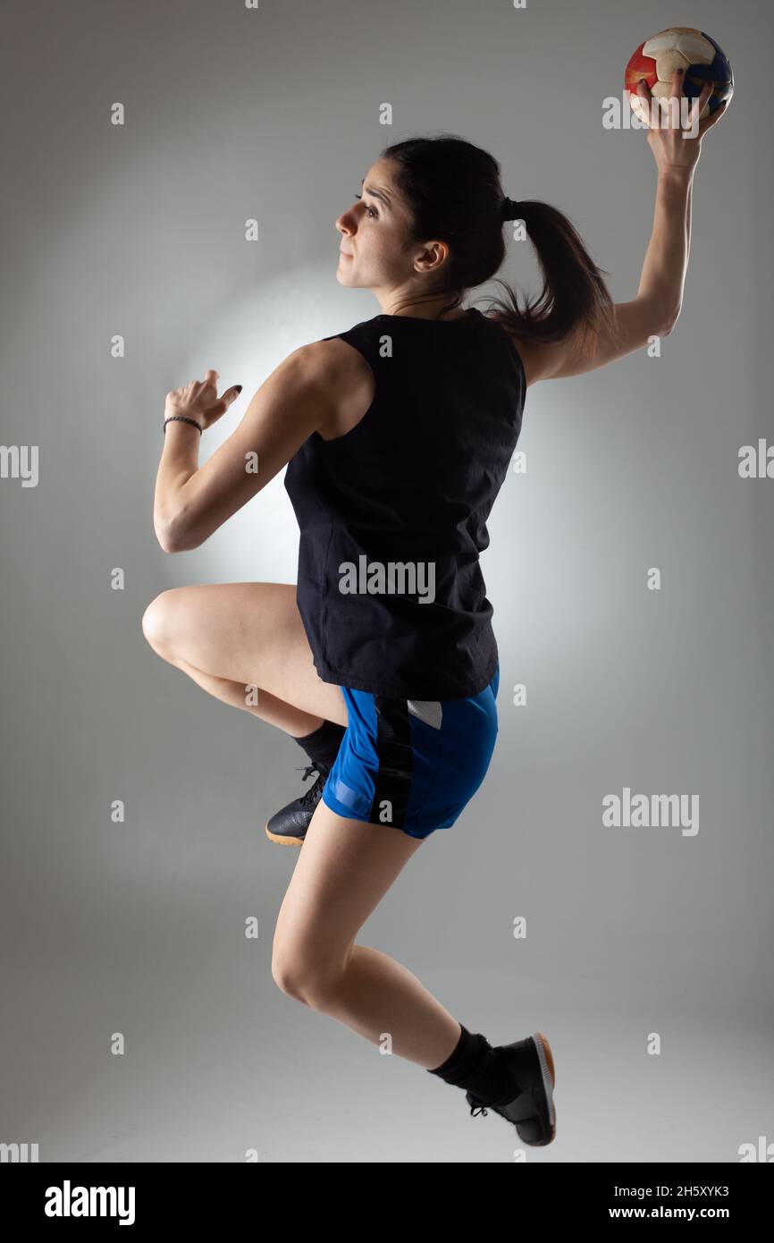 Handball player posing on light gray background. Girl jumping with ball ...